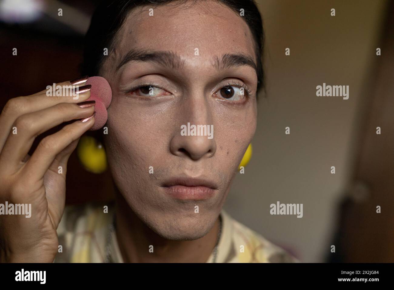 A transgender young man (22) is in his room putting on makeup. Concept ...