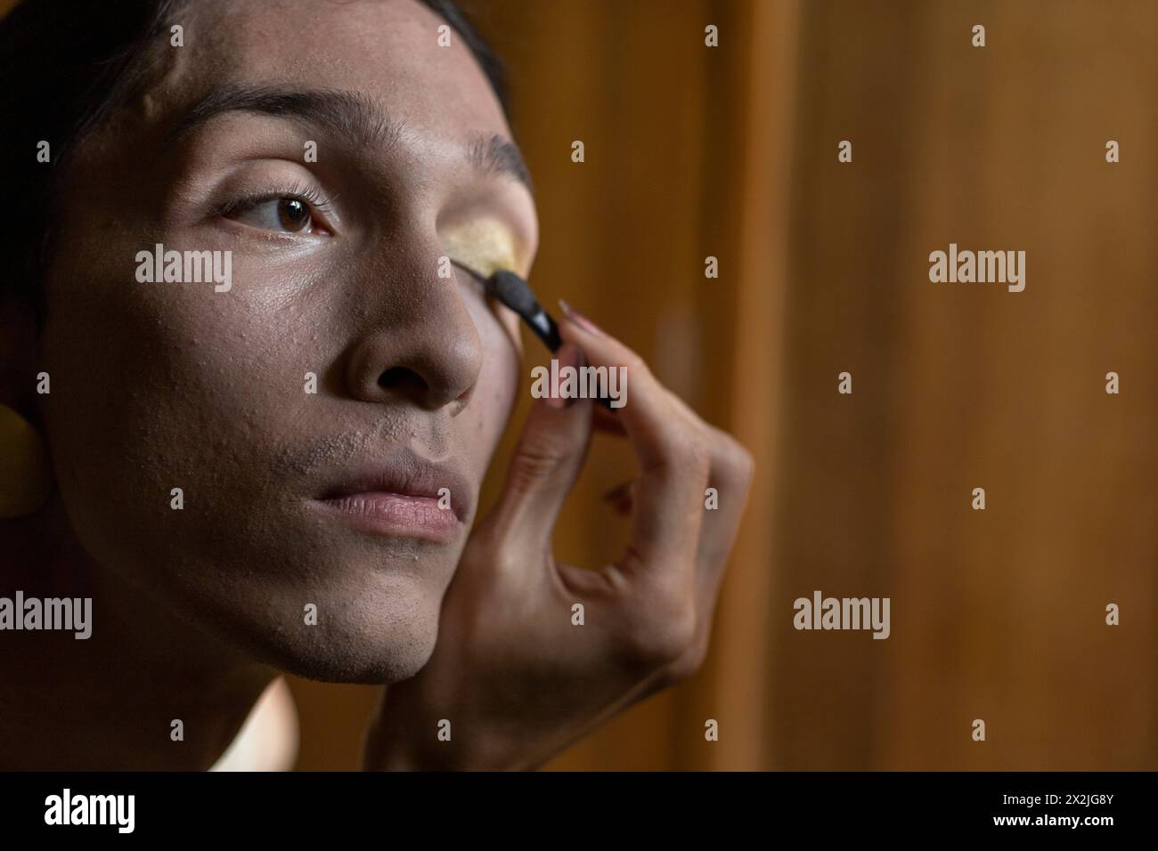 A transgender young man (22) is in his room putting on makeup. Concept ...