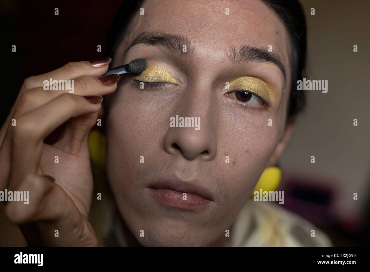 A transgender young man (22) is in his room putting on makeup. Concept ...