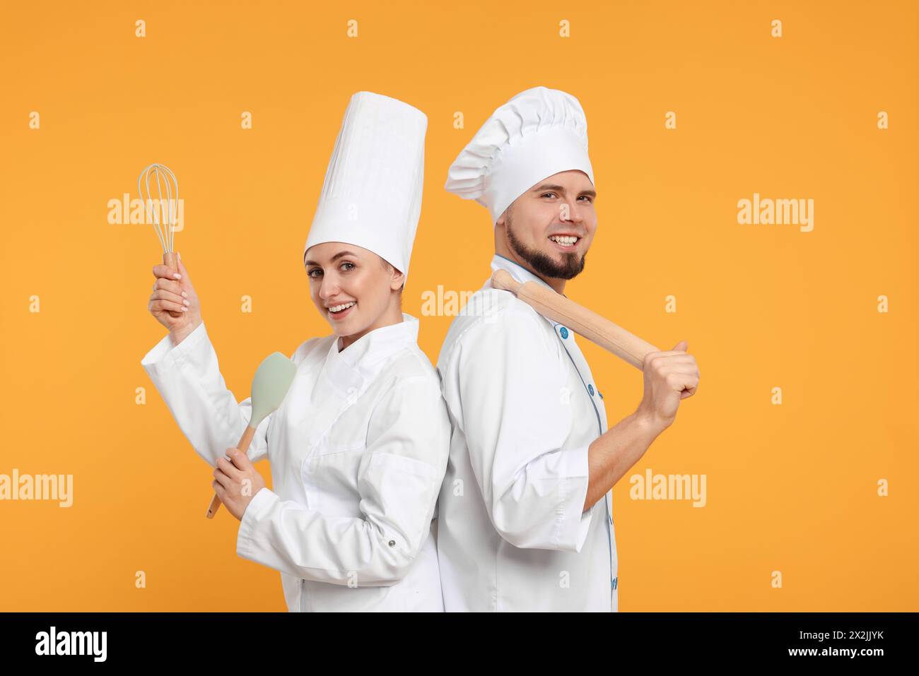 Happy confectioners in uniforms holding professional tools on yellow ...