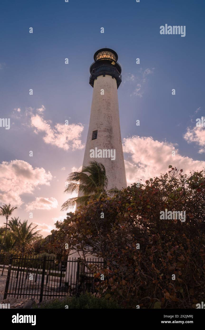 A white lighthouse against deep blue sky with white clouds tinted with ...