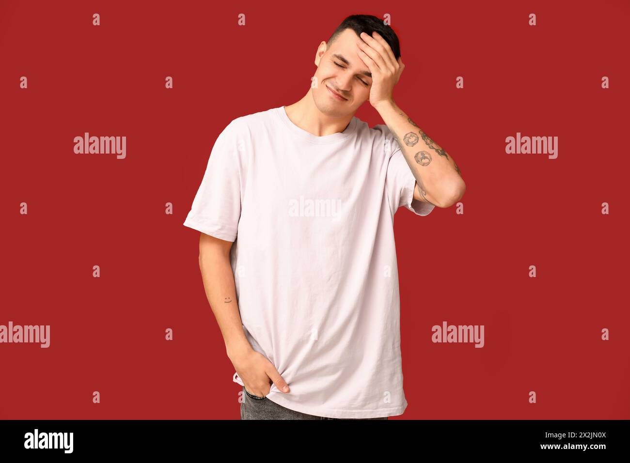 Handsome ashamed young man covering face with hand on red background ...