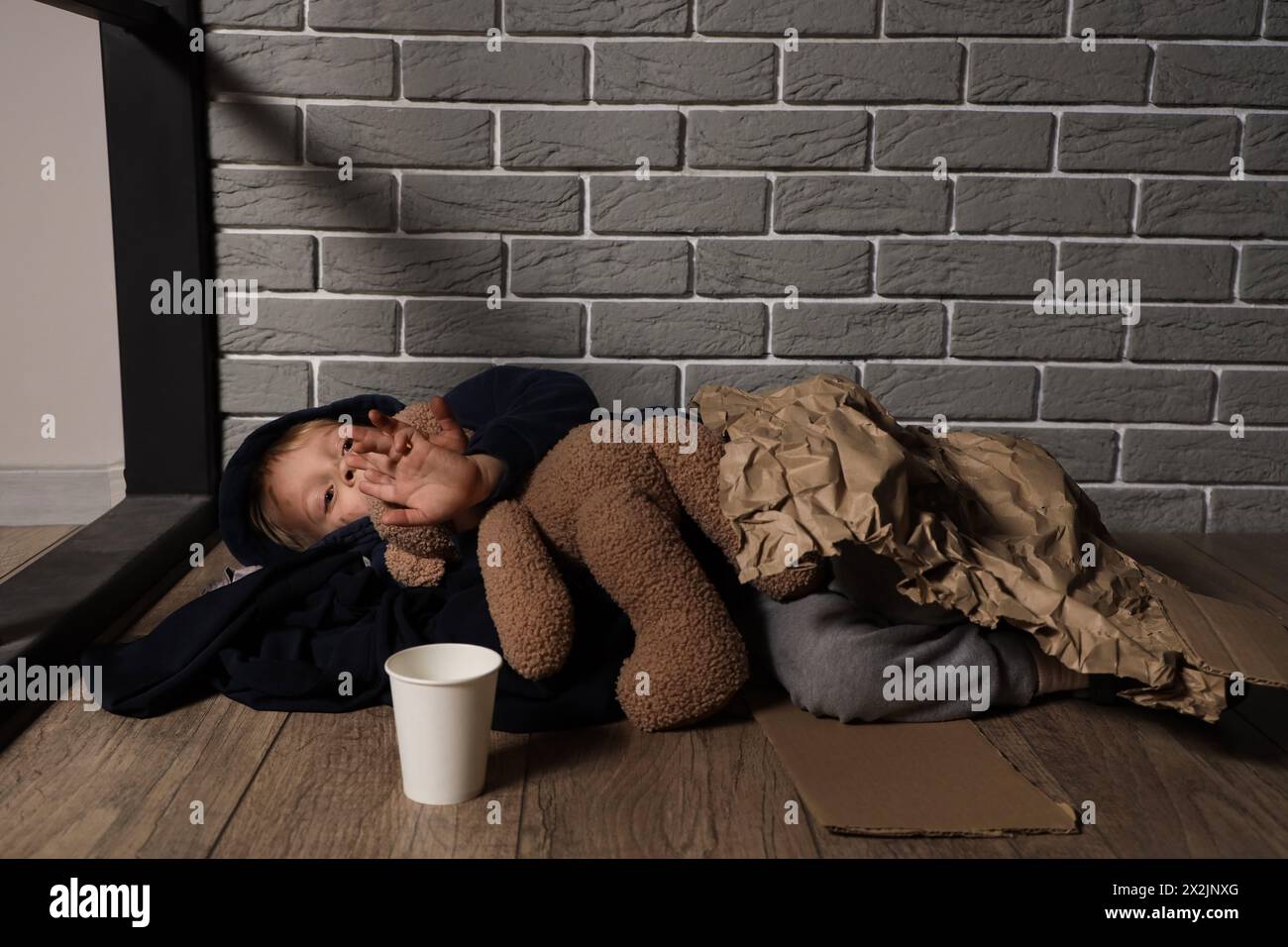 Homeless little boy with toy bear lying near grey brick wall Stock ...