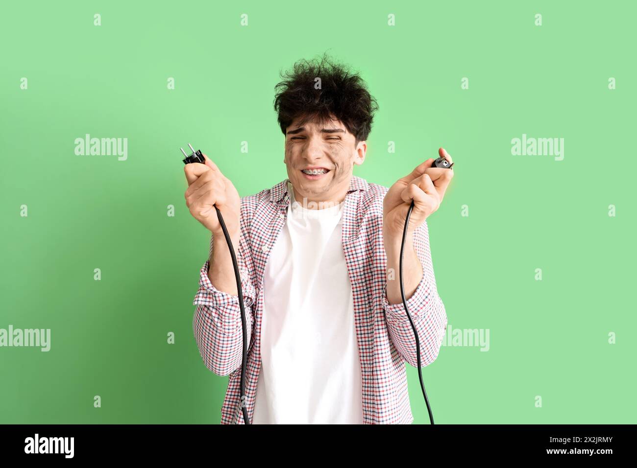 Electrocuted young man with burnt face and plugs on green background ...