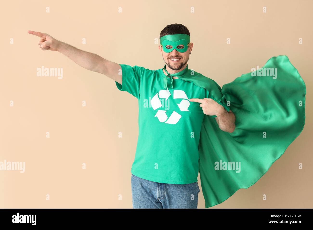 Young man dressed as eco superhero pointing at recycling logo on his t ...