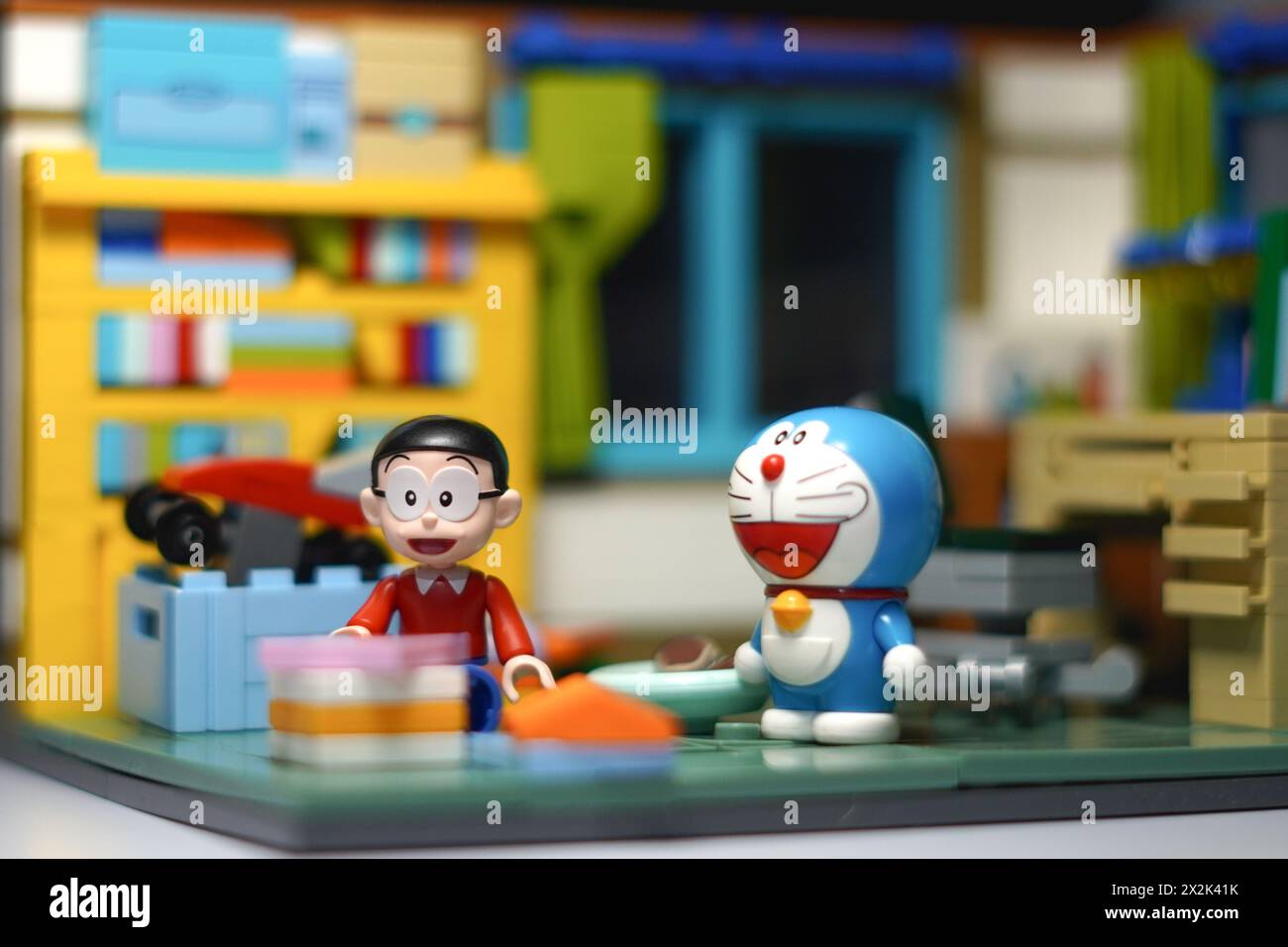 Japanese toy figures (Nobita and Doraemon) sitting near a pile of books ...