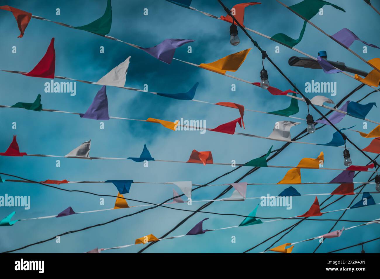 A vibrant display of colorful flags strung across light bulbs under a ...