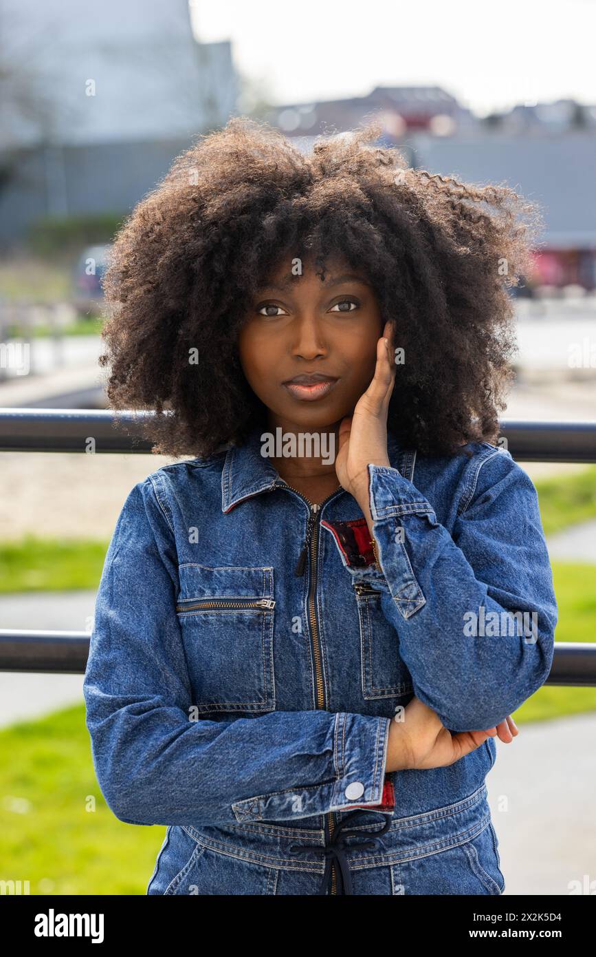 This image portrays a young Black woman leaning against a railing on a ...