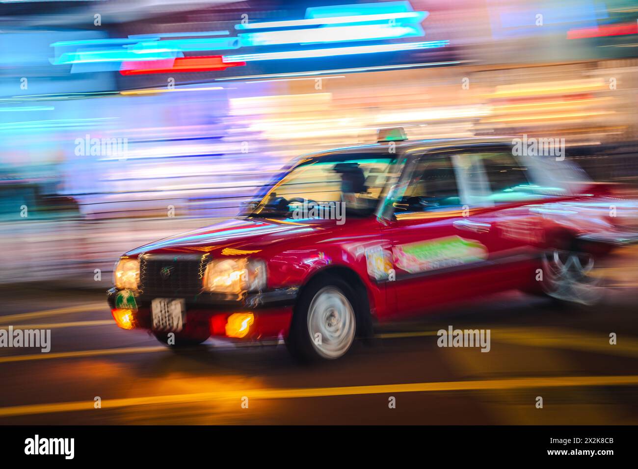 A red taxi captured in motion at night, with city lights creating a ...