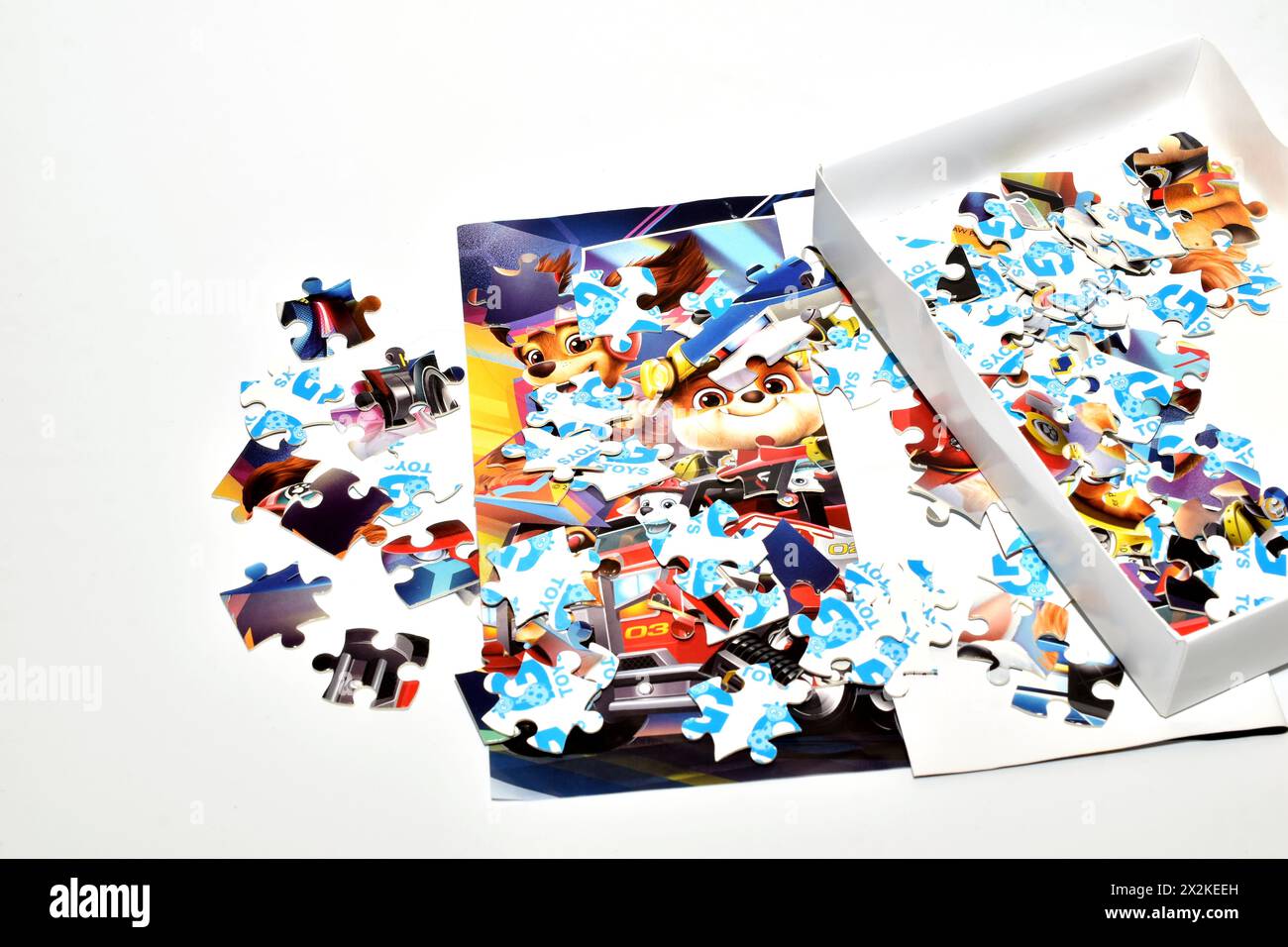 On a white background there are puzzles scattered from the box and a ...