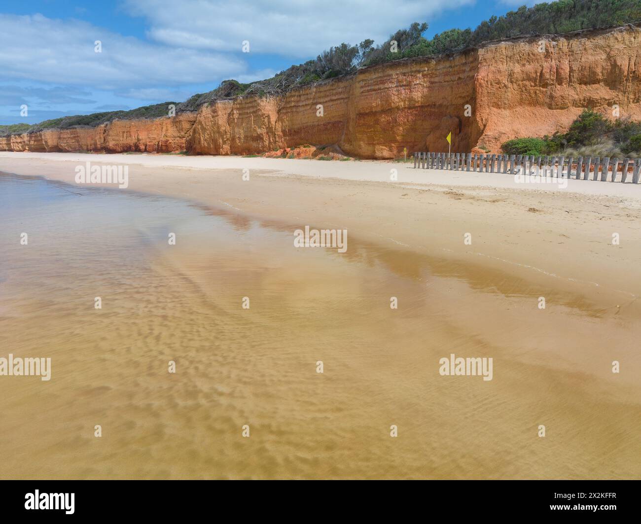 Low angled view of shallow waves on a sandy beach below high sea cliffs ...