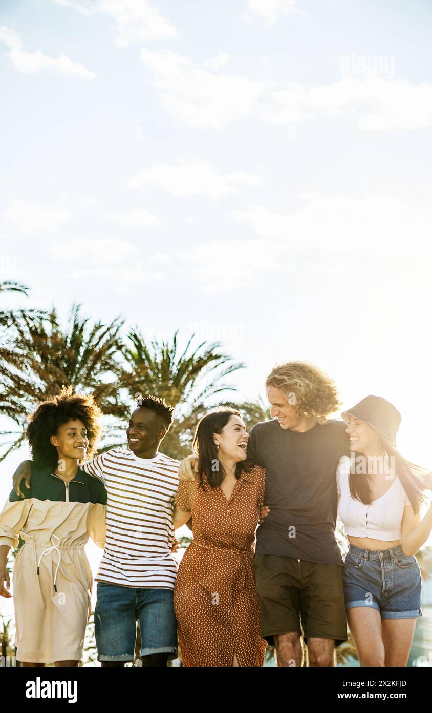 Millennial group of friends walking embraced while laughing outdoors in ...