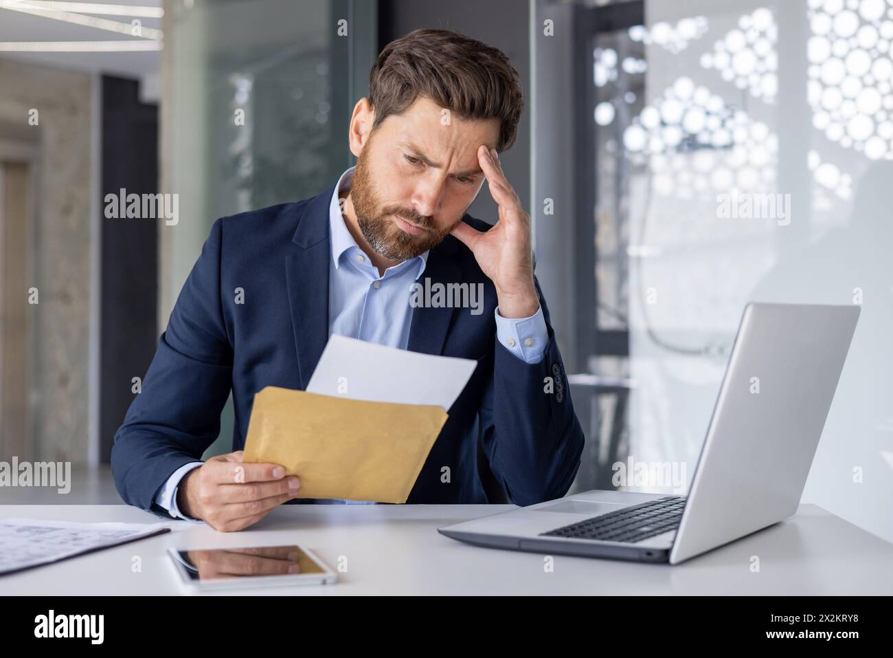 Stressed businessman in a suit appears troubled while reading a letter ...