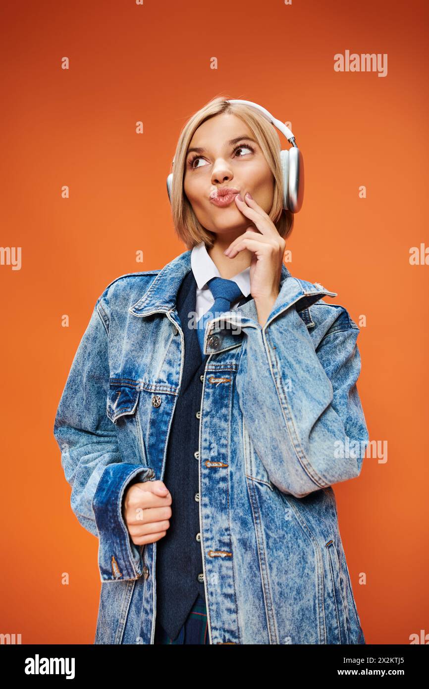 joyous young woman with blonde hair with headphones in denim jacket ...