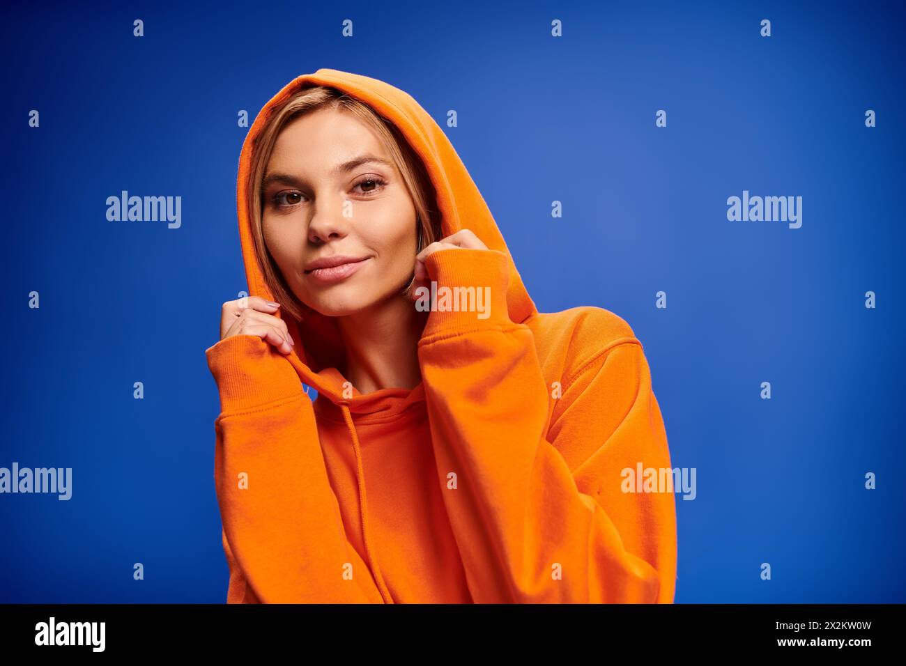 Beautiful Jolly Woman With Blonde Short Hair In Vivid Attire With Hood On Posing On Blue