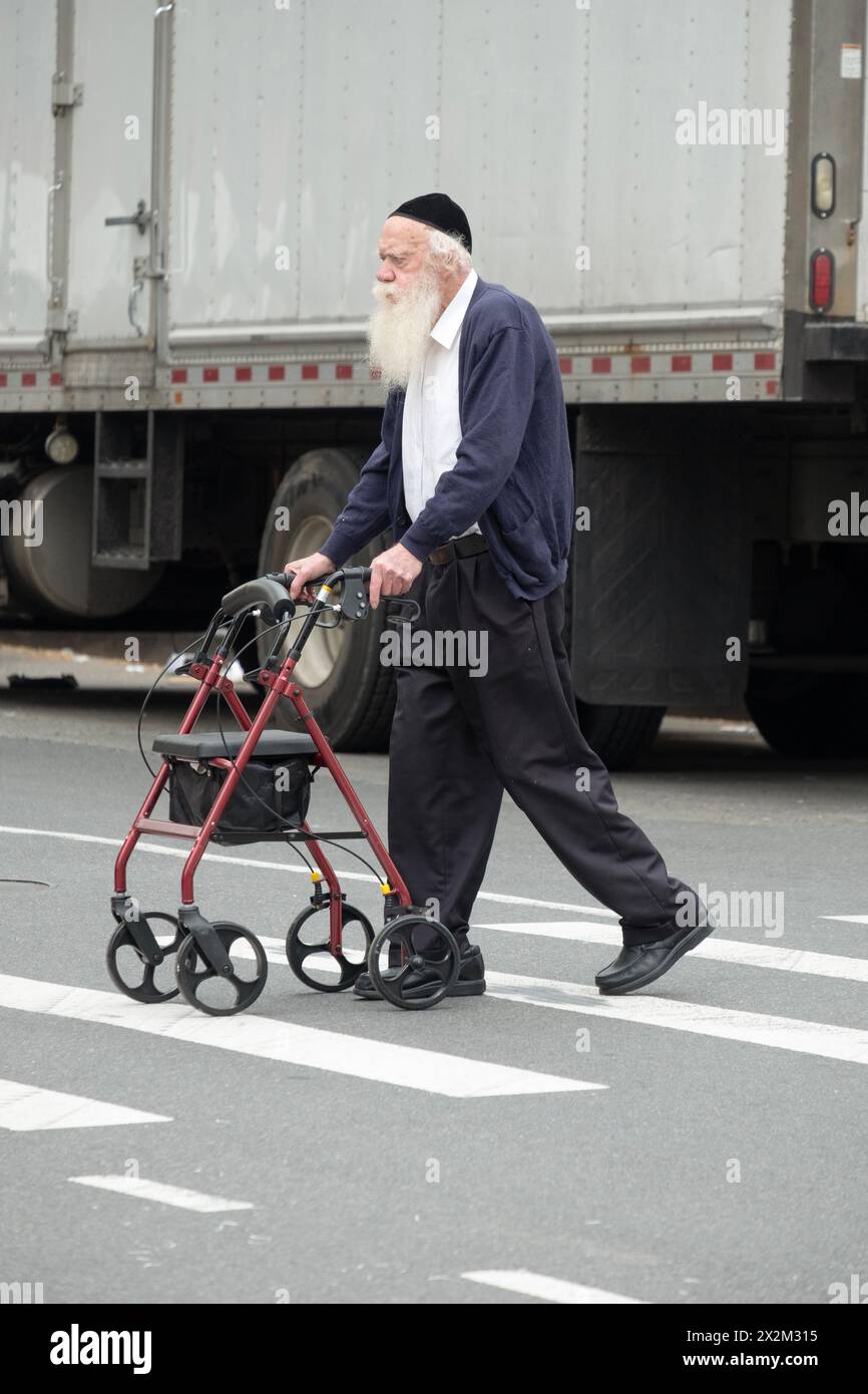 An older hasidic Jewish man crossing a street while pushing a walker ...