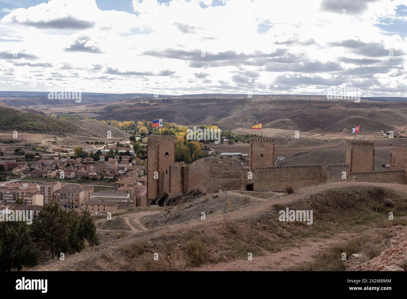 ancient stone castle with three flags, overlooking a town in a valley ...