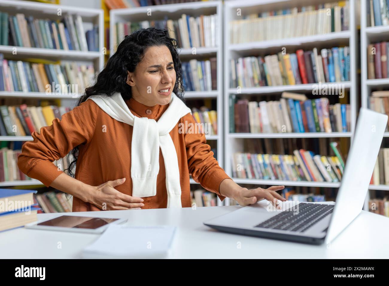 A young female student in a library clutching her stomach in pain ...
