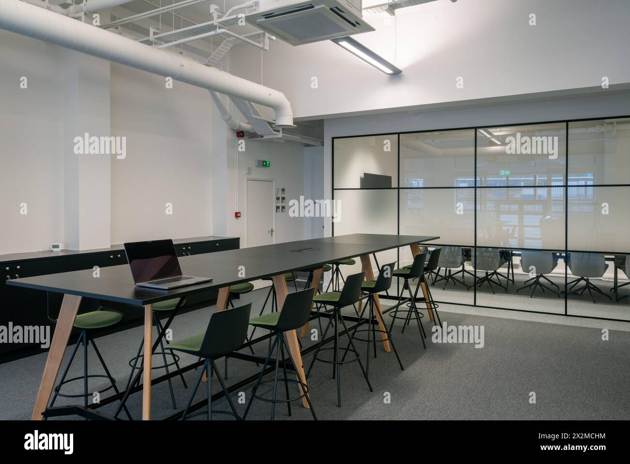 A contemporary meeting room in an office, equipped with a long table, chairs, and a laptop ...