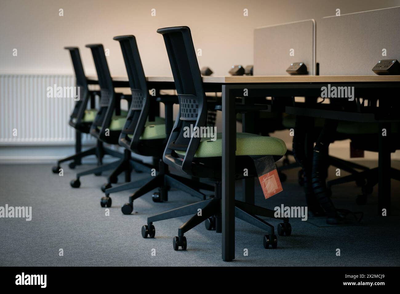 A line of black ergonomic office chairs in front of desks with ...