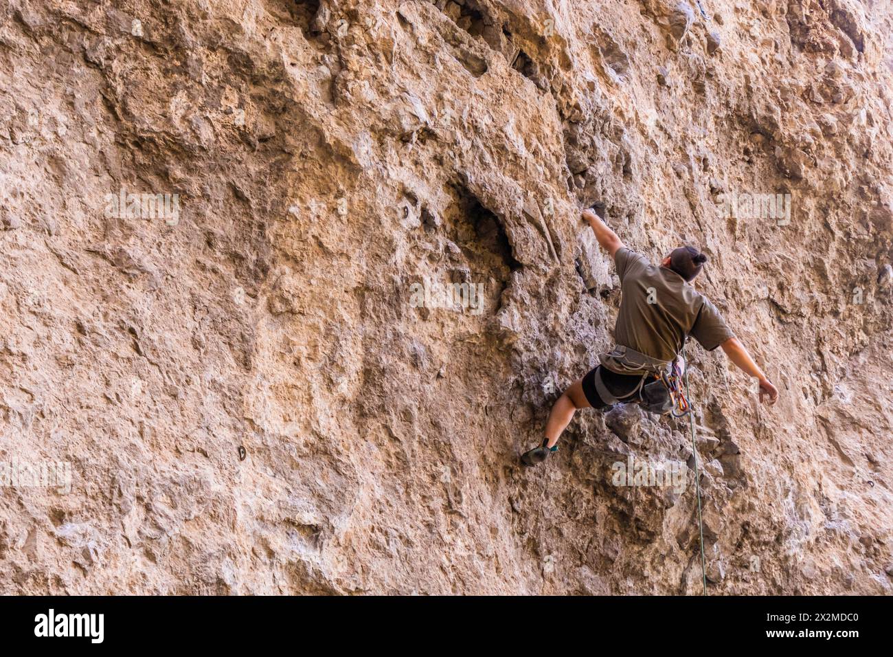 An intrepid climber ascends a steep and craggy rock face, equipped with ...