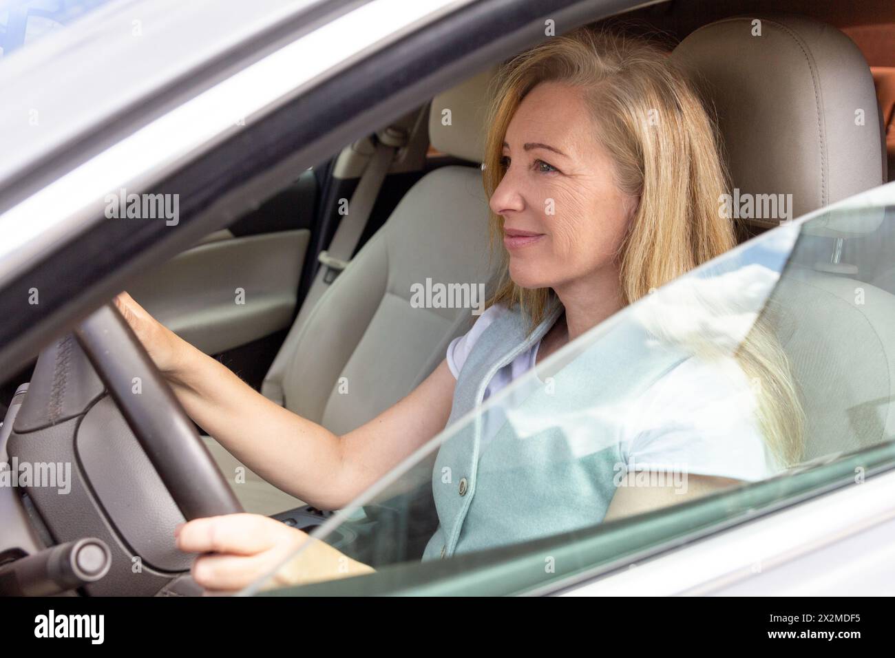 A content middle-aged woman is behind the wheel, driving her car with ...