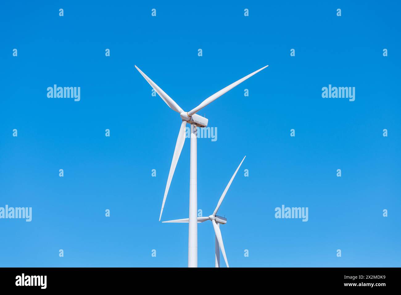 Two white wind turbines tower against a clear blue sky, symbolizing ...