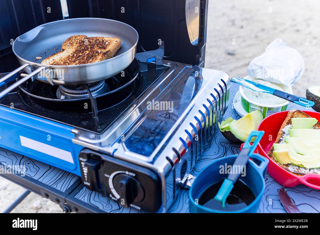 Portable gas stove cooking toast with avocado breakfast at a campsite ...