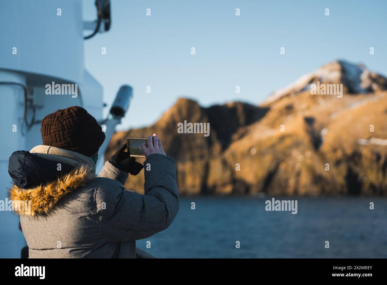 A person clad in warm attire takes a photo of Iceland's rugged ...