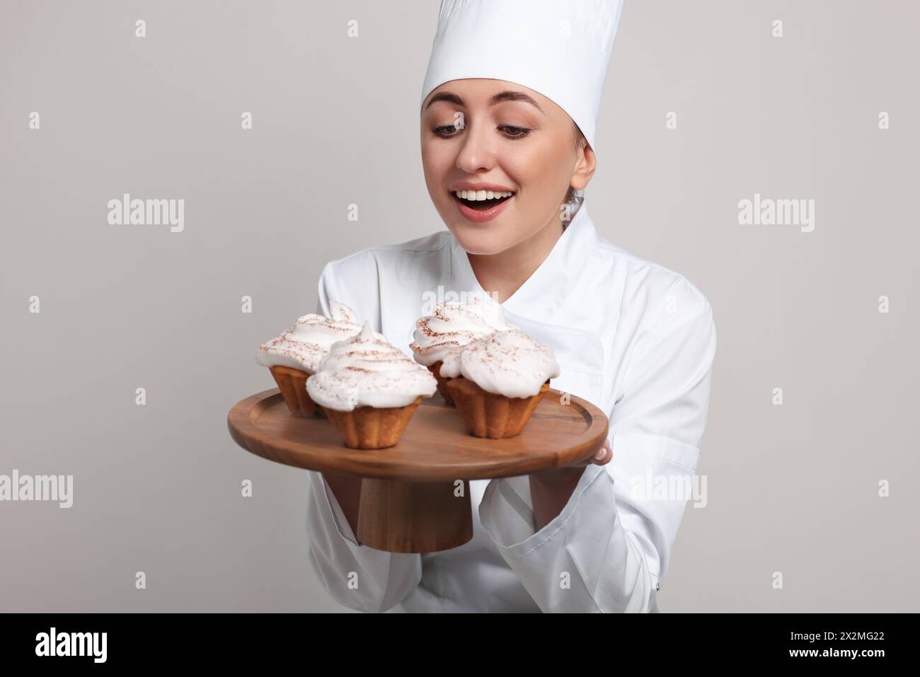 Happy professional confectioner in uniform holding delicious cupcakes ...