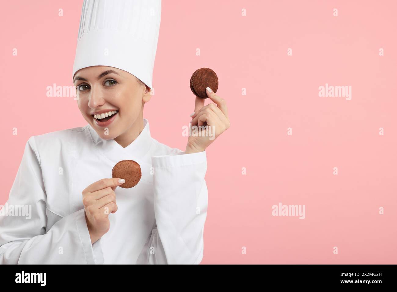 Happy professional confectioner in uniform holding delicious macarons ...