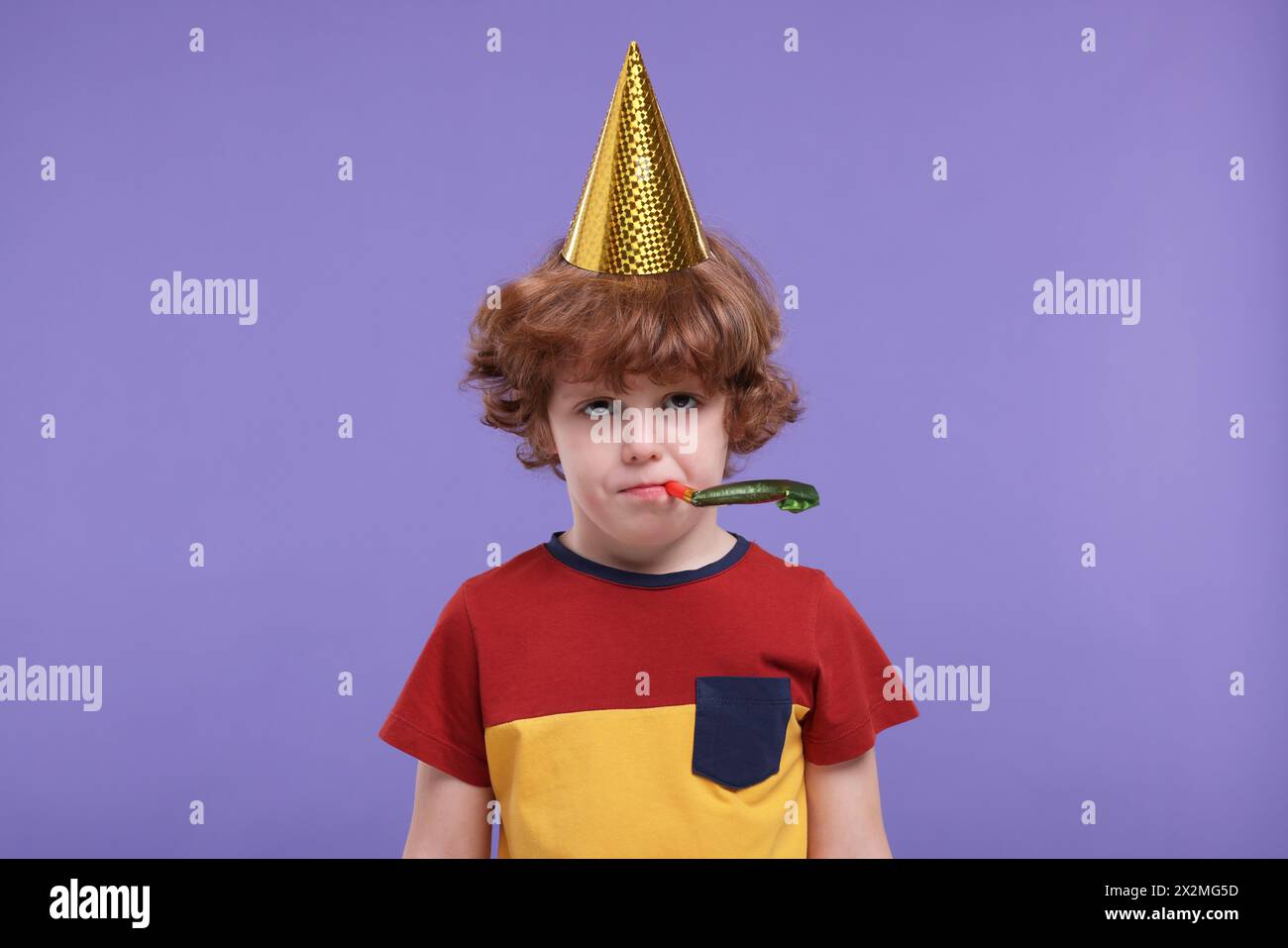 Sad little boy in party hat with blower on purple background Stock ...