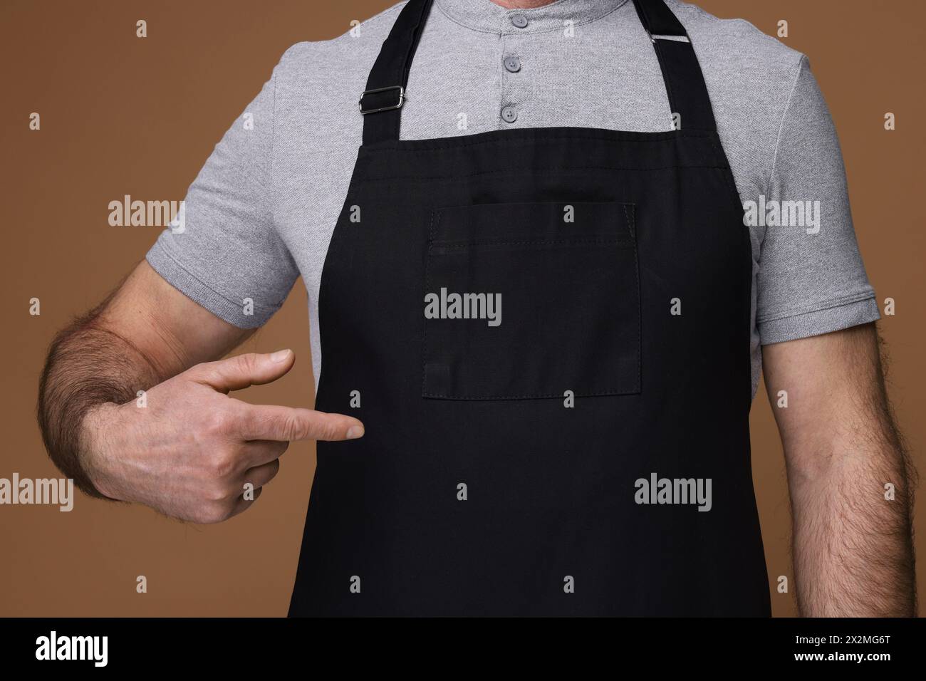 Man pointing at kitchen apron on brown background, closeup. Mockup for ...