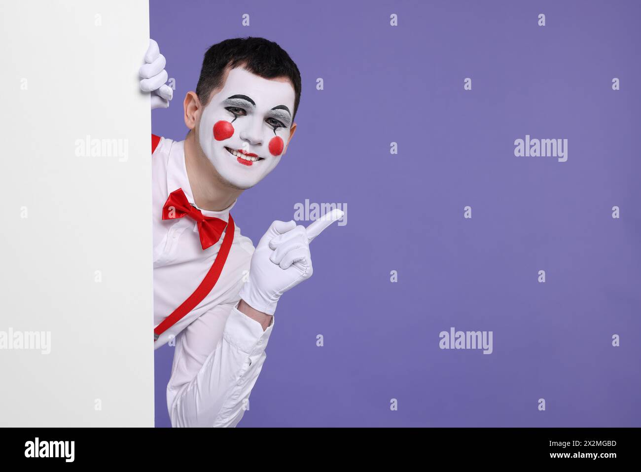 Funny mime artist peeking out of blank poster and pointing at something ...