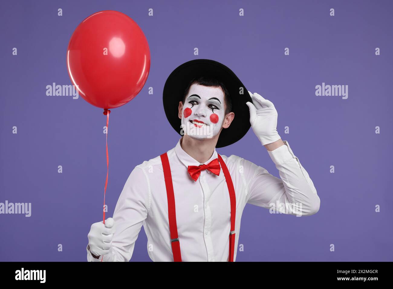 Funny mime artist with red balloon on purple background Stock Photo - Alamy