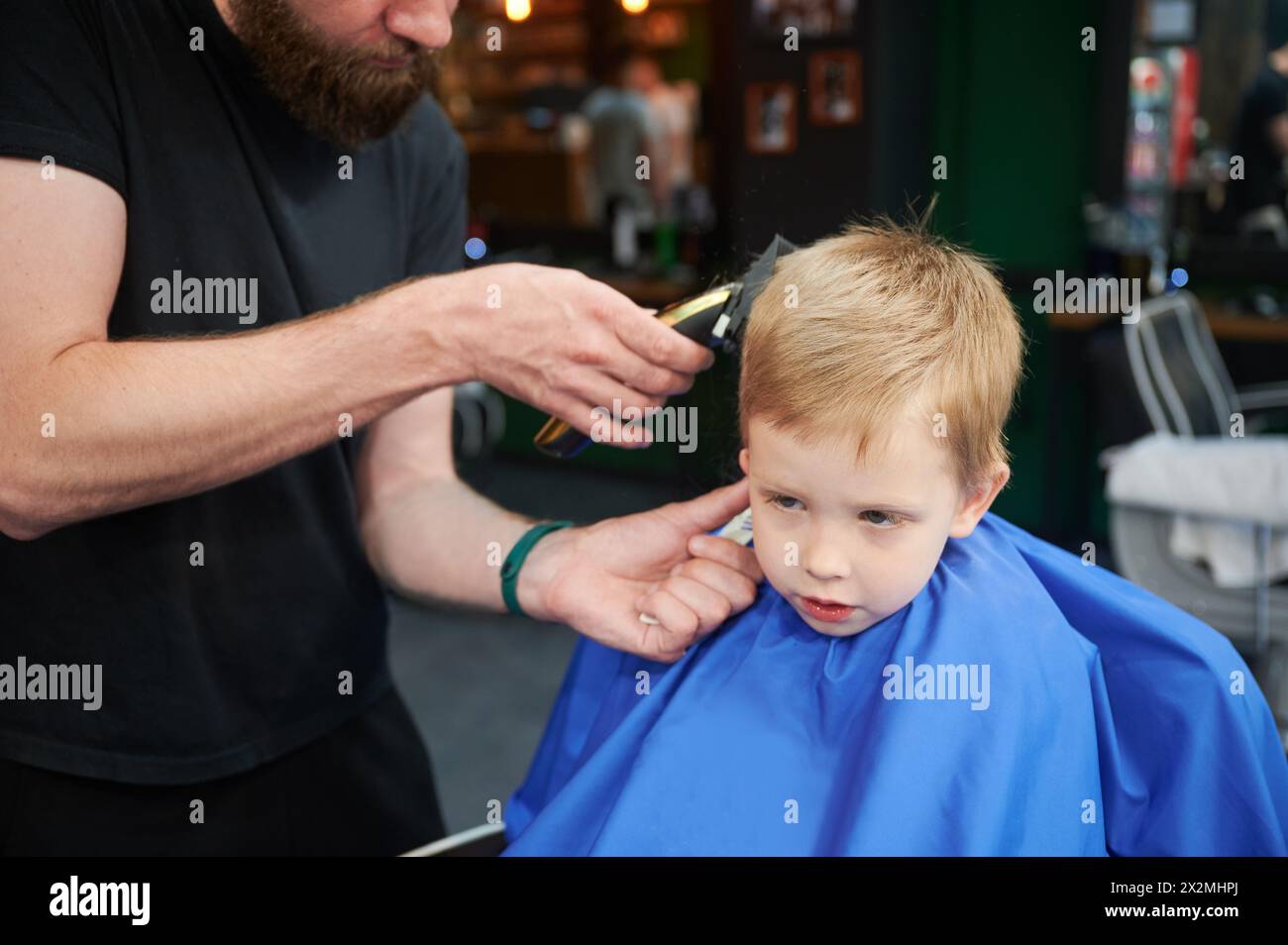 Hairdresser using electric shaver to cut boy's hair. Little kid getting ...