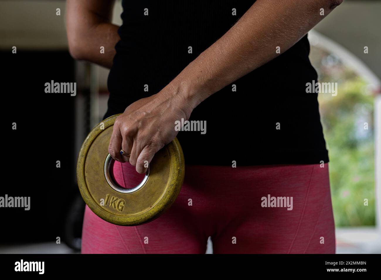 Latin American woman holds a dumbbell in her hand as she performs arm ...