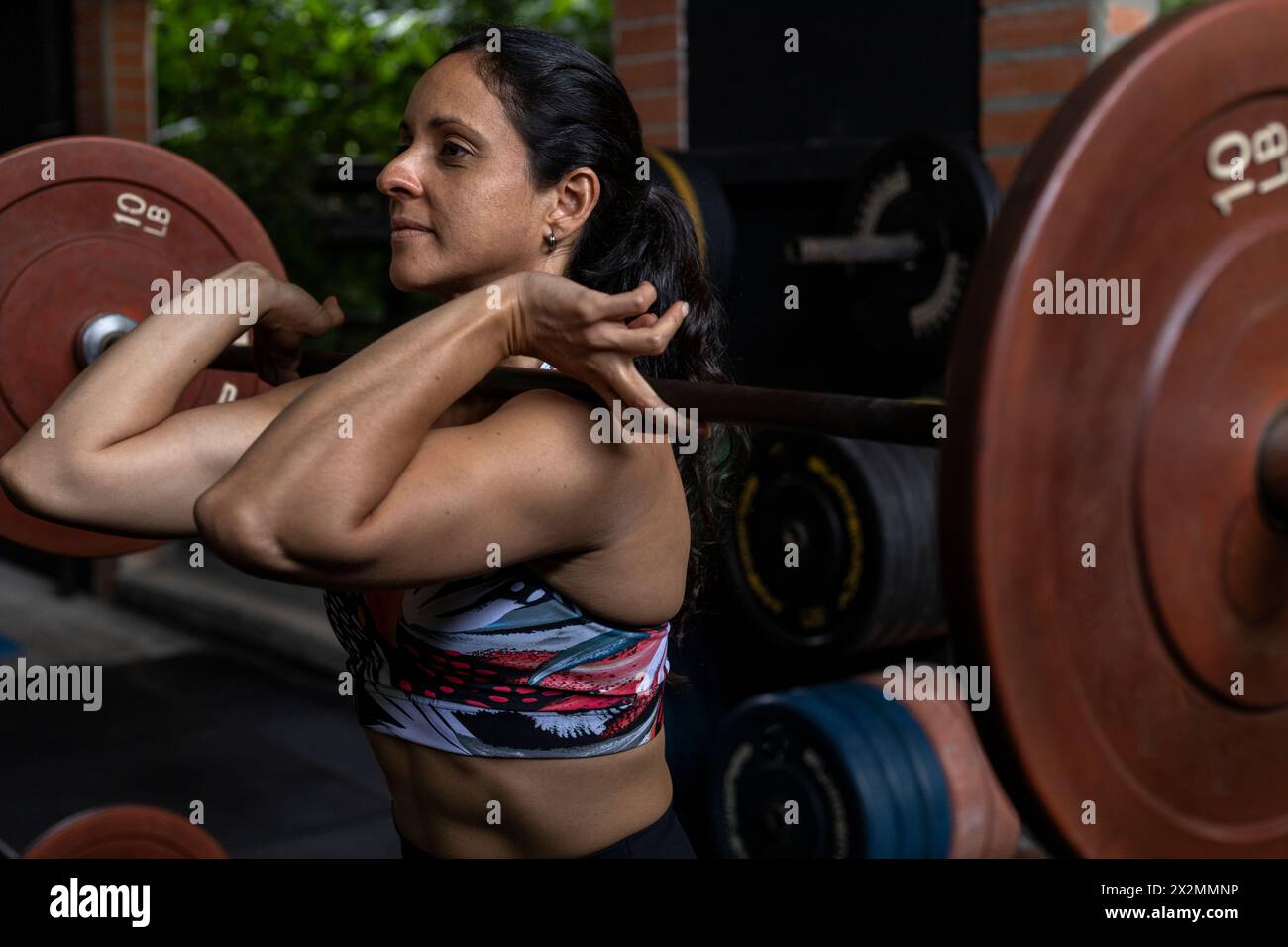 Latin American woman standing holding a barbell with weights on her ...