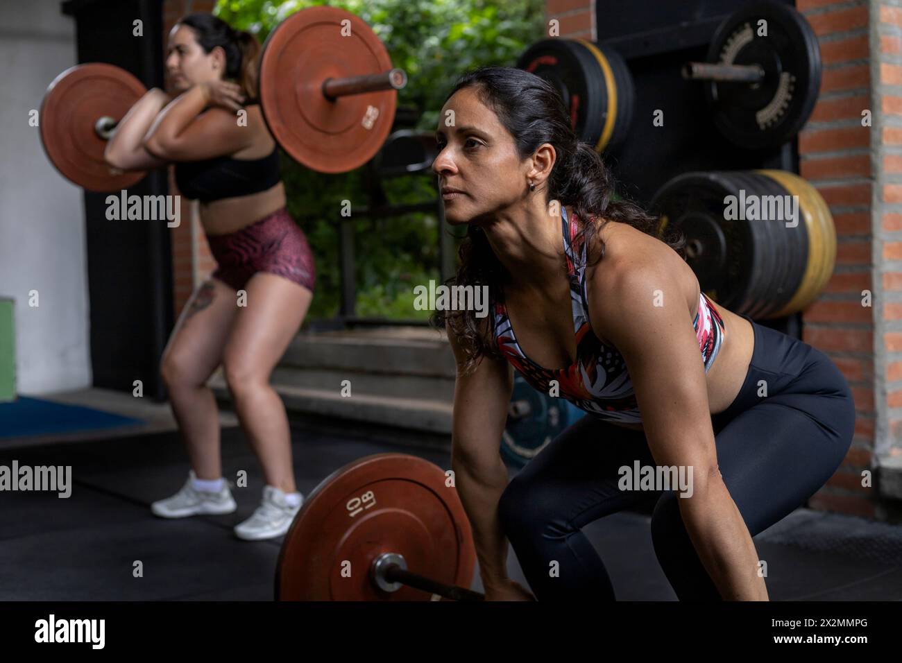 Two Latin American women perform functional workouts executed at high intensity in the gym using ...