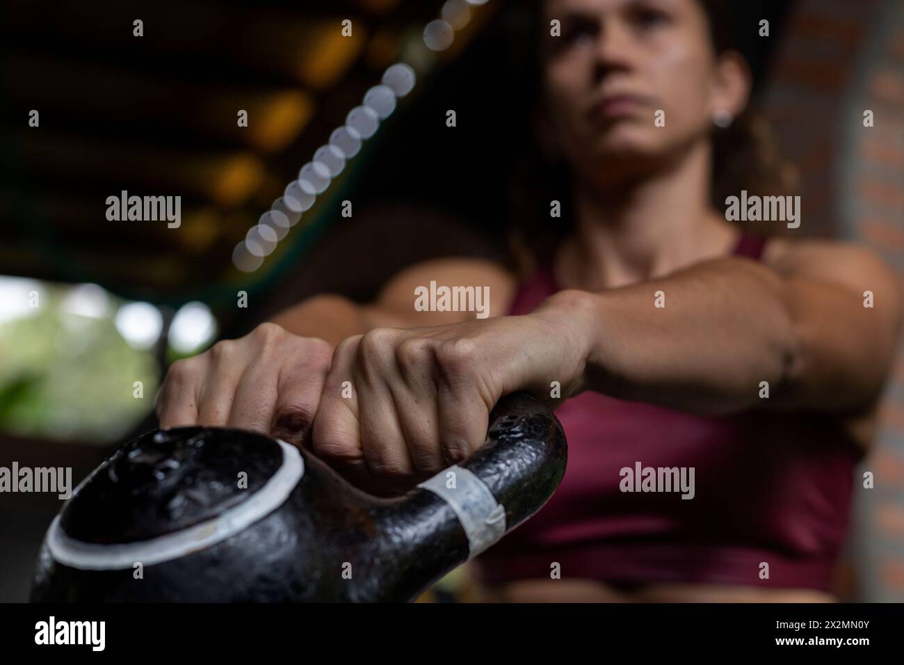Latin American woman lifts a kettlebell with both hands during her high ...