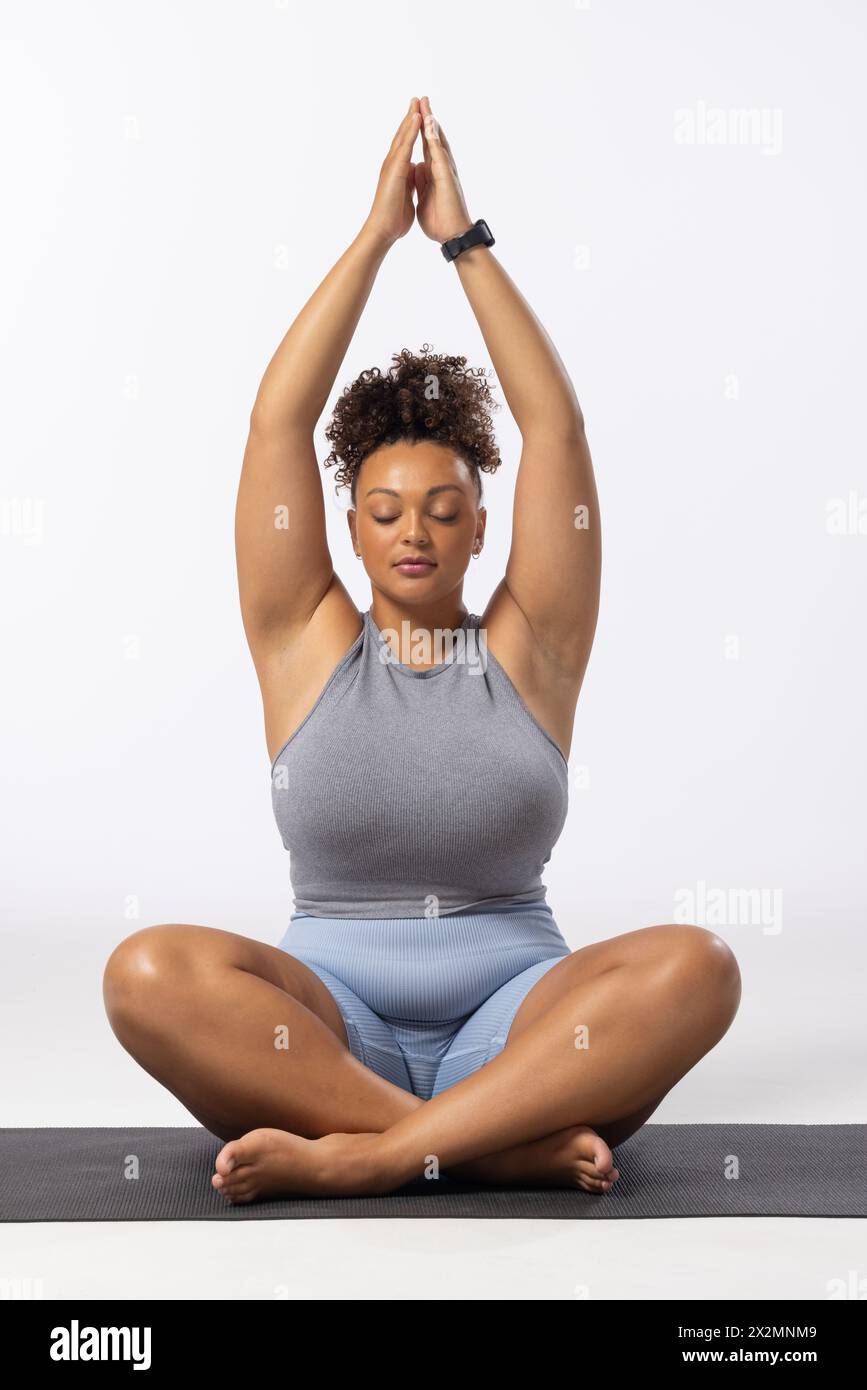 A biracial young female plus size model practices yoga on white ...