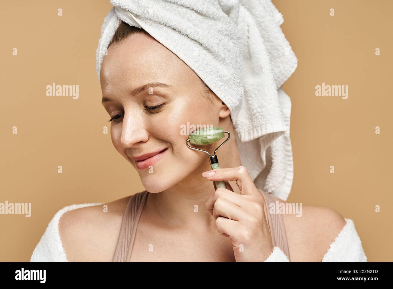 A graceful woman with a towel on her head is seen holding face roller ...