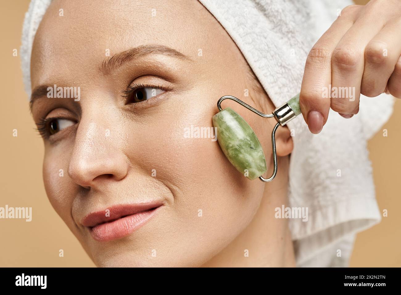 A beautiful woman with a towel on her head is playfully holding gua sha ...