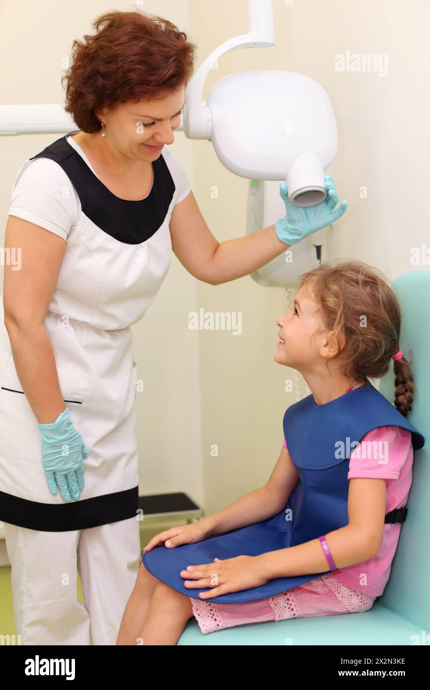 Dentist prepares smiling girl wearing in protective lead apron to jaw x ...