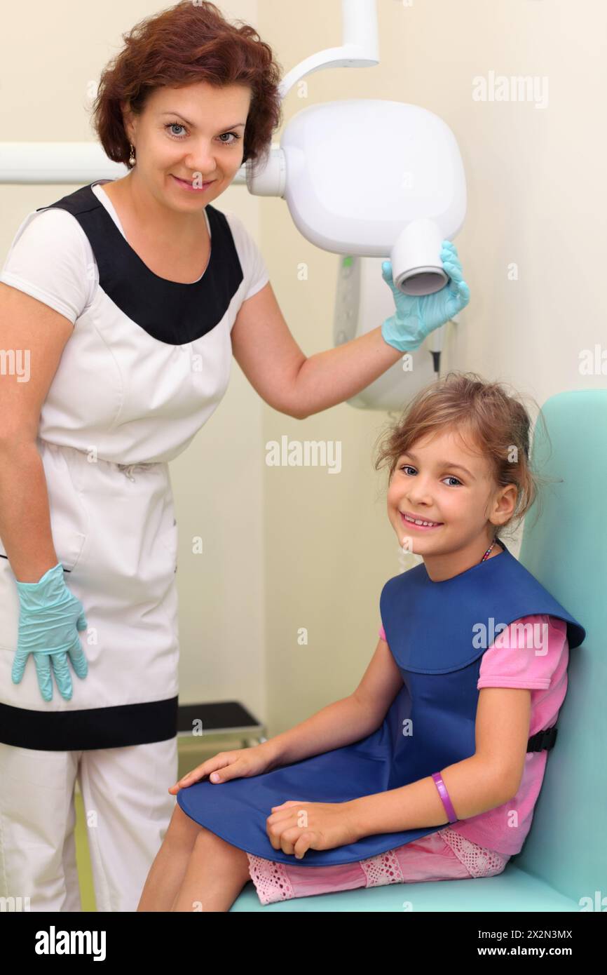 Dentist prepares smiling girl wearing in protective lead apron to jaw x ...