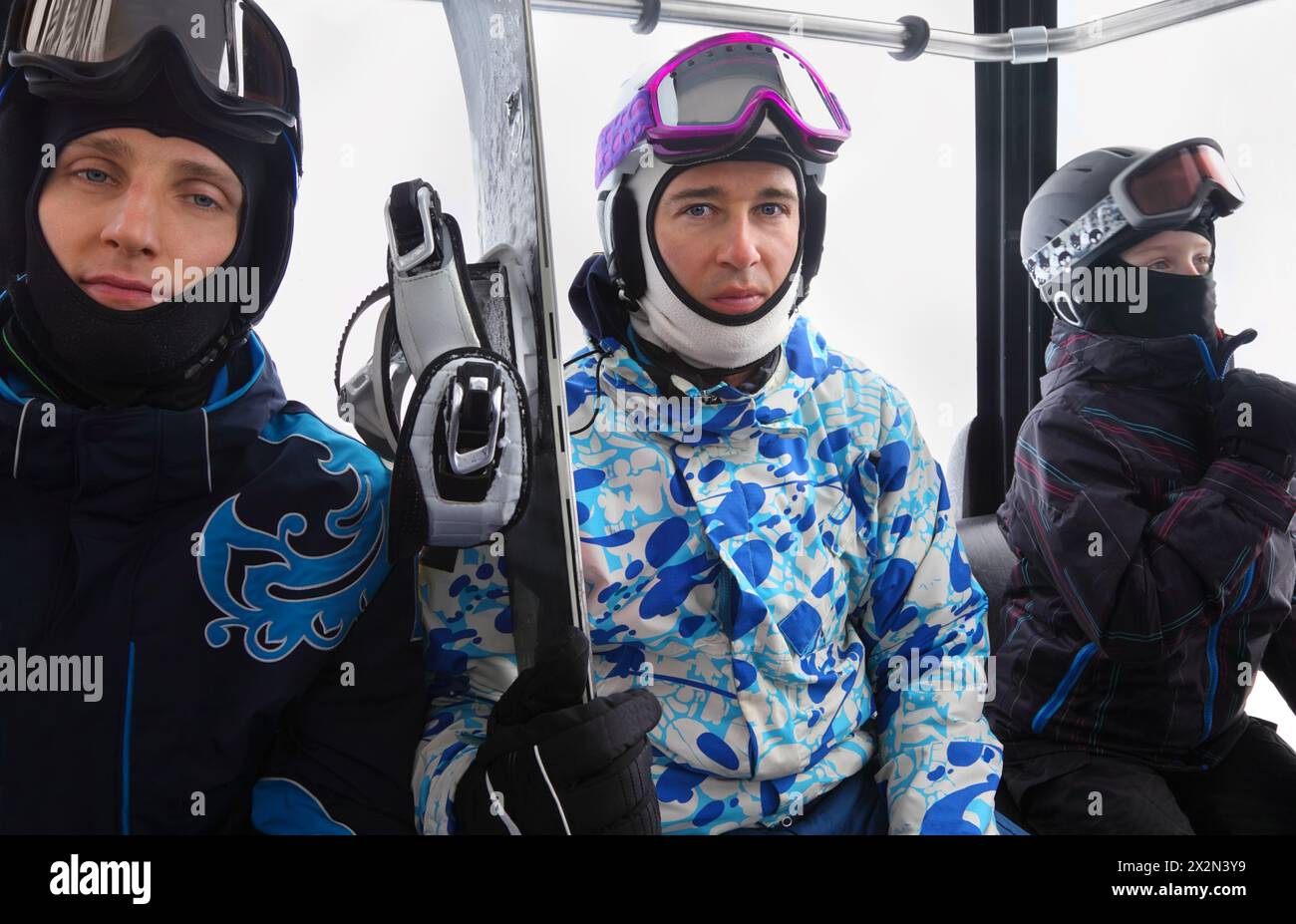 Three skiers in helmets ride on funicular in mountains. Focus on middle ...