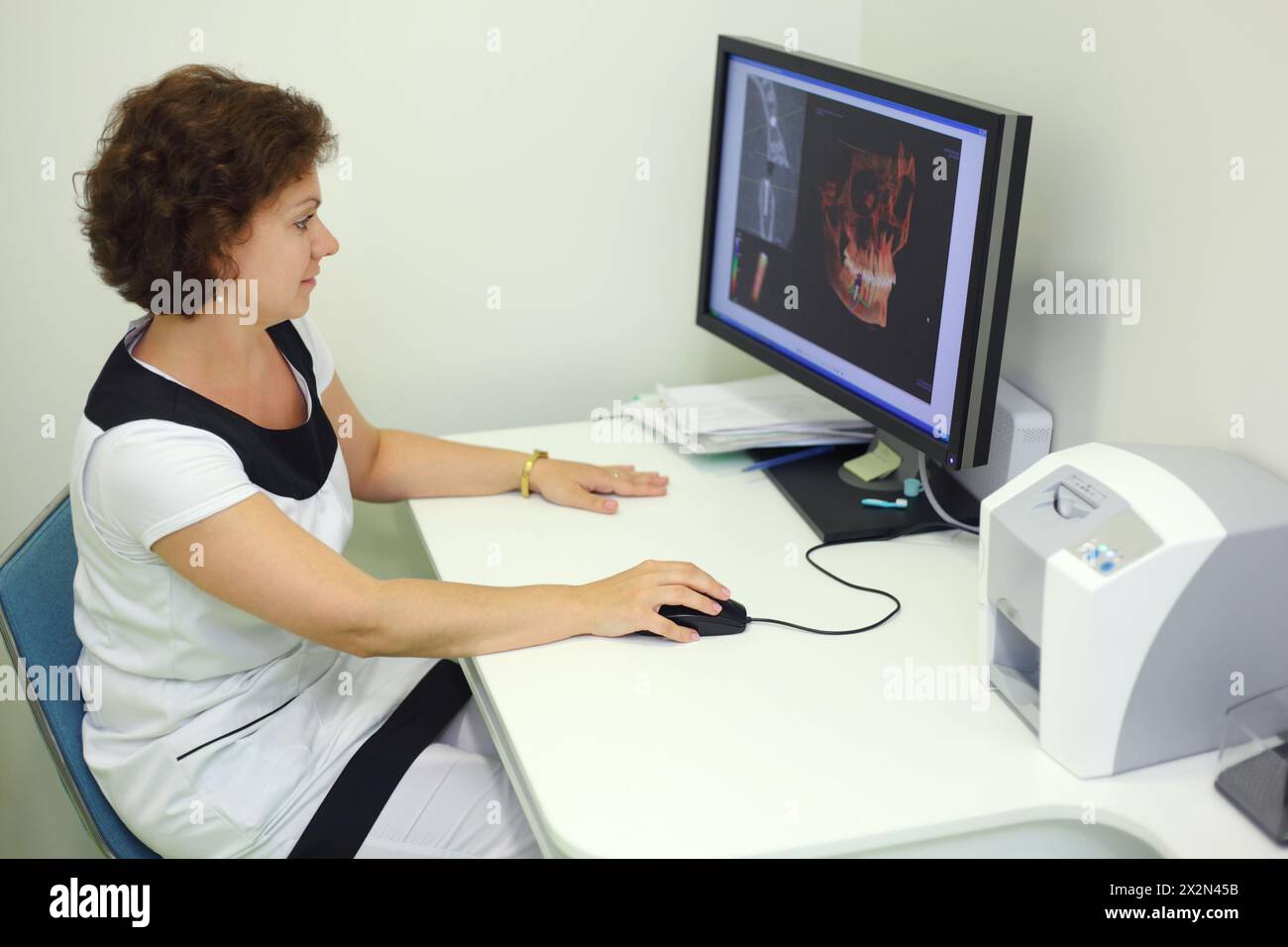 Dentist carefully looks skull X-rays at computer monitor in dental ...