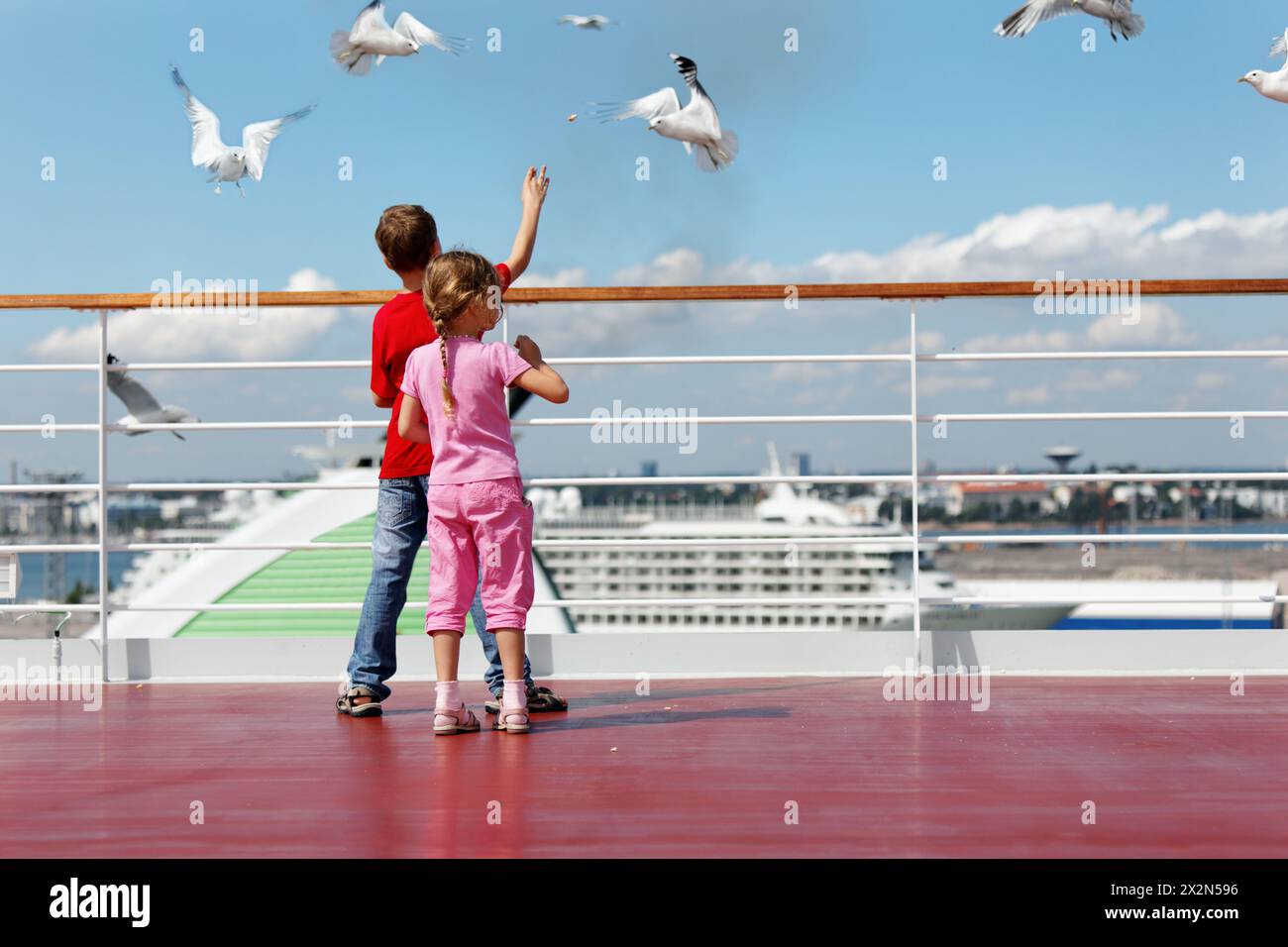 Boy in red t-shirt and his younger sister feed seaguls on deck of ship ...
