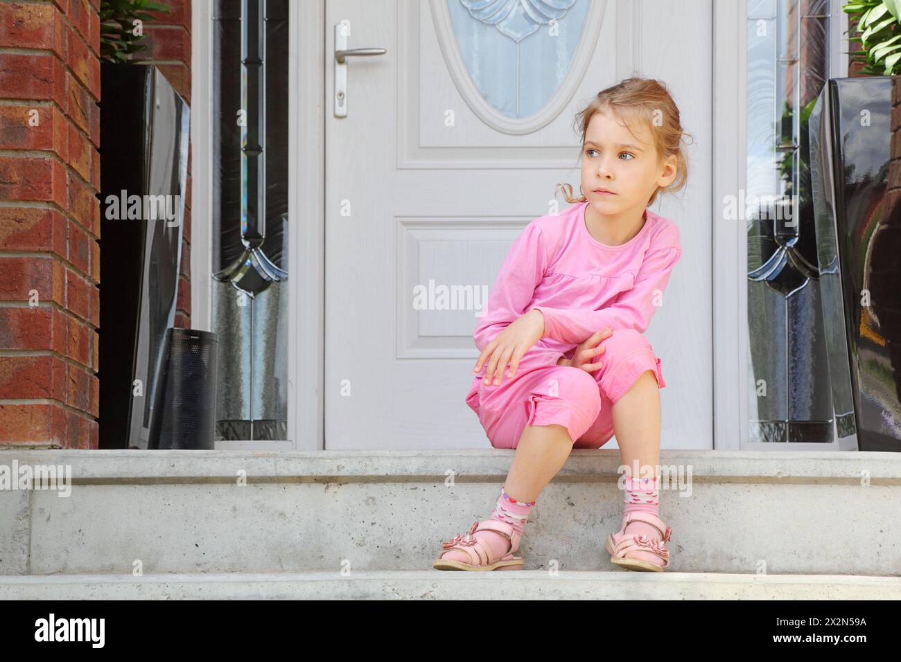 Little awake girl sits on stairs near door and looks away Stock Photo ...