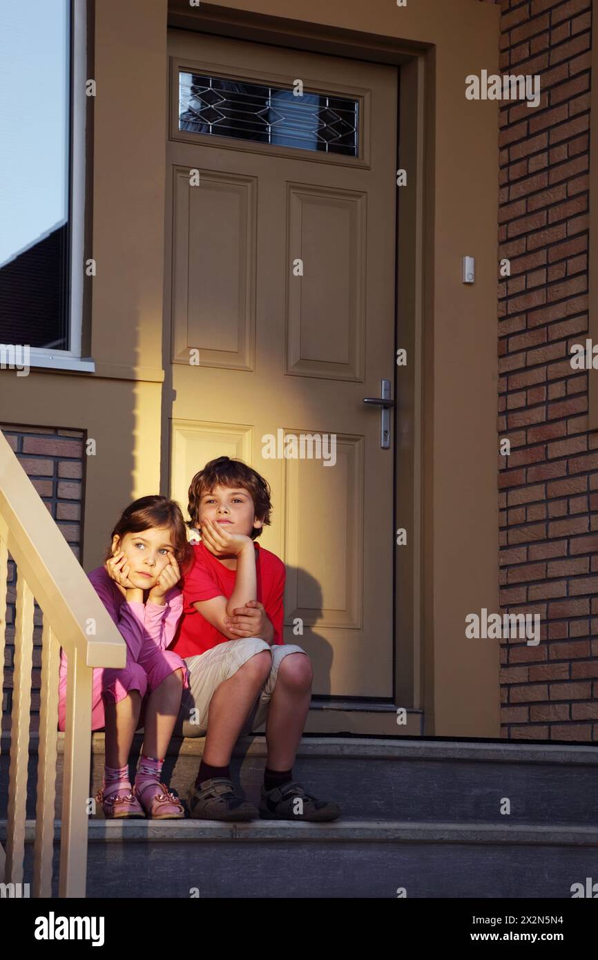 Brother and sister sit on stairs near door and look into distance at ...